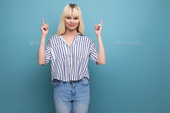 smiling positive blond young woman in striped shirt pointing finger at ...