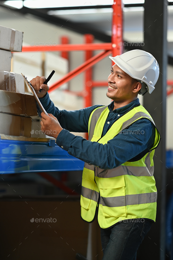 Smiling asian male worker checking quantity of storage product on ...