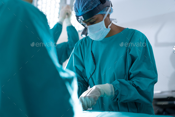 Diverse surgeons wearing surgical gowns operating on patient in ...