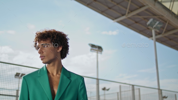 Curly student looking camera at stadium fashion portrait. Serious model ...
