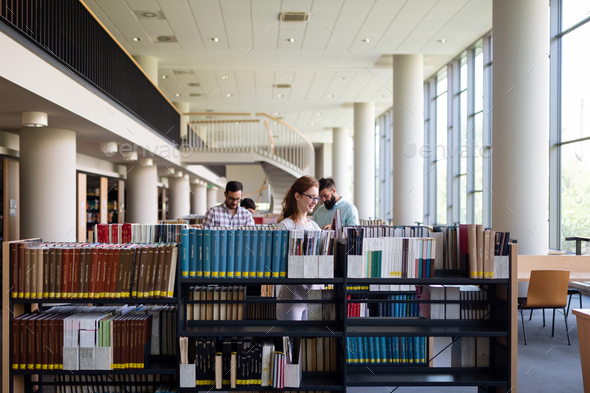 Happy young university students studying with books in library. Group ...
