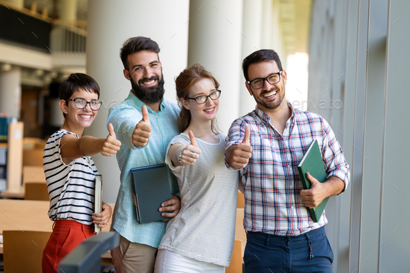 Happy university students studying with books in library. Group of ...