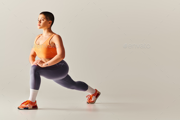 body positivity movement, young short haired woman doing lunges on grey ...