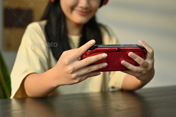 Smiling asian girl playing video game on a portable game console at ...