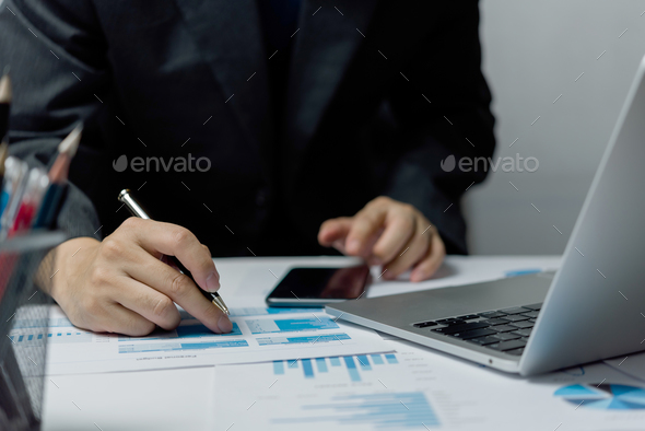Businessperson reviewing documents with pen, analyzing data on graph ...