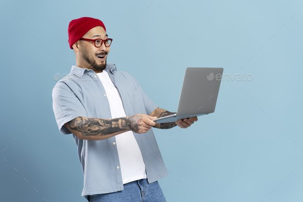 Excited stylish asian man holding laptop computer, watching videos with ...