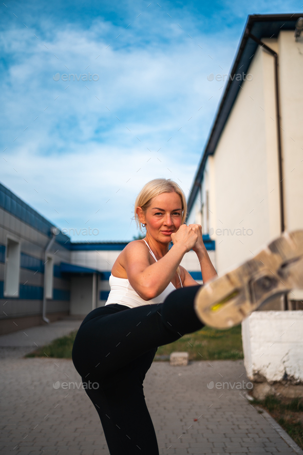 Adult beautiful blonde woman doing box kicks exercises workout outdoors ...