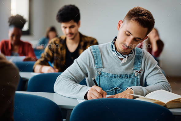 Male student taking notes while learning at university classroom. Stock ...