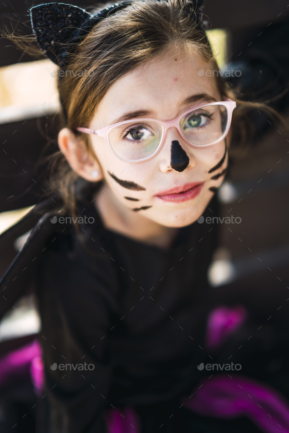 Portrait of a cute little girl wearing a Halloween cat costume with her ...