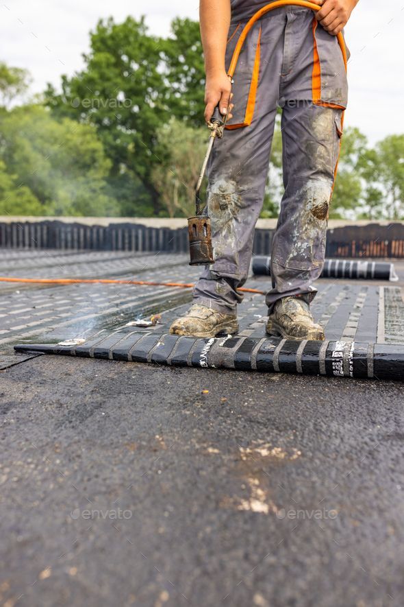 Worker placing a vapor barrier on the roof using a propane gas torch ...