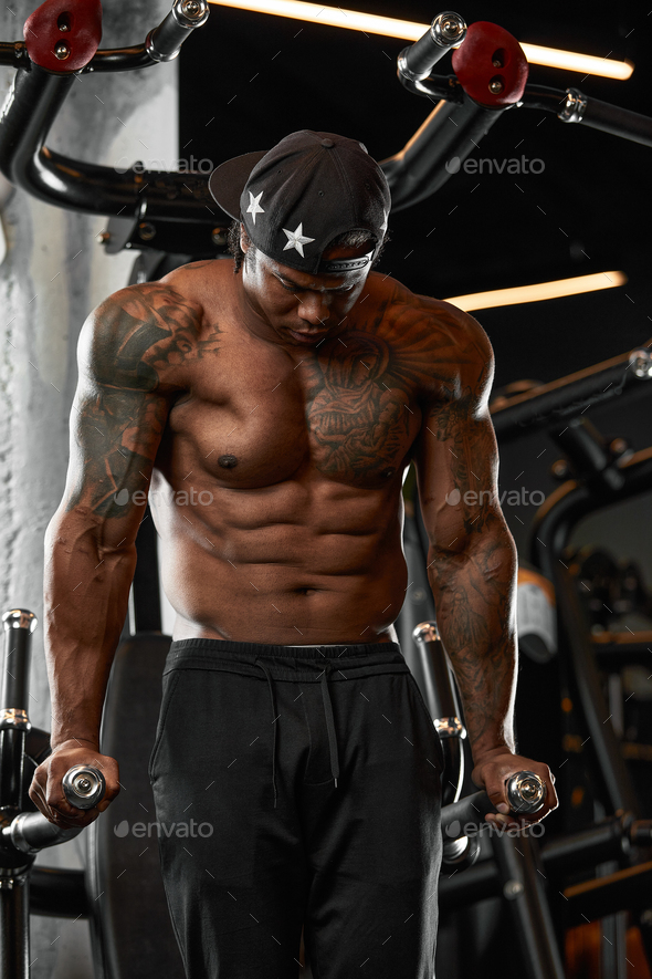 Strong and muscular dark skin man trains on modern equipment in gym ...