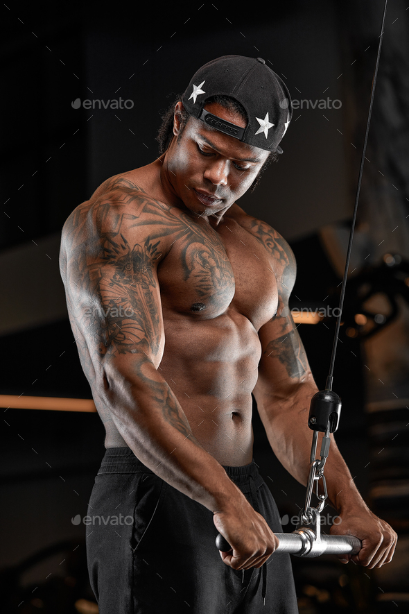 Strong and muscular dark skin man trains on modern equipment in gym ...