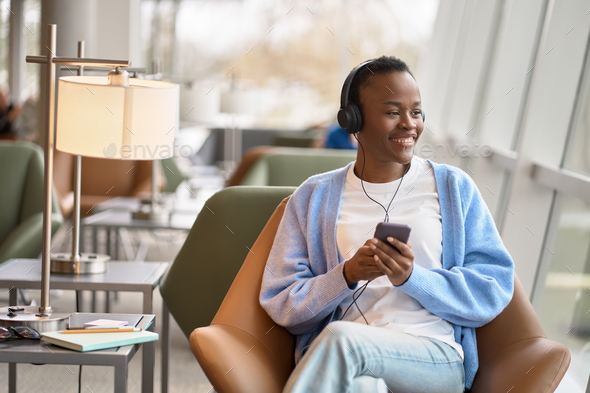 Smiling African generation z girl wearing headphones using smartphone ...