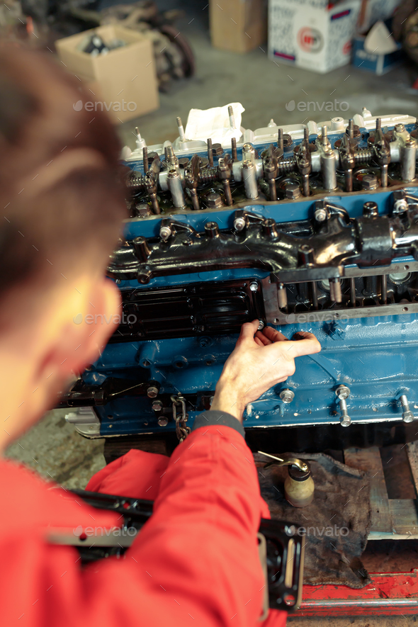 Vertical closeup of a mechanic in a red uniform mounting the car engine ...