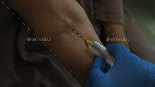 Hand with gloves inserting vacutainer to a person for blood extraction ...