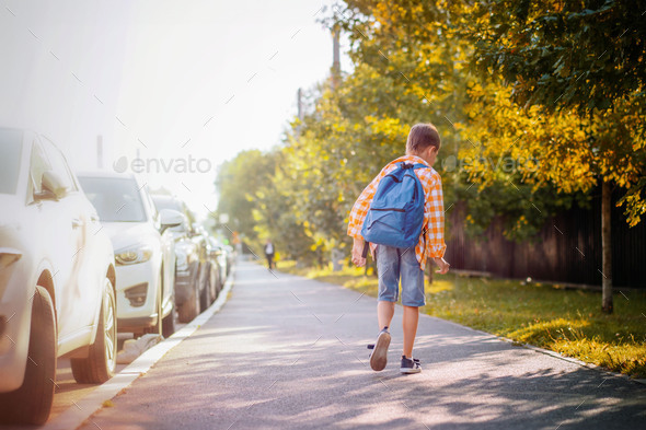 back view of caucasian boy walking from school wearing school bag ...