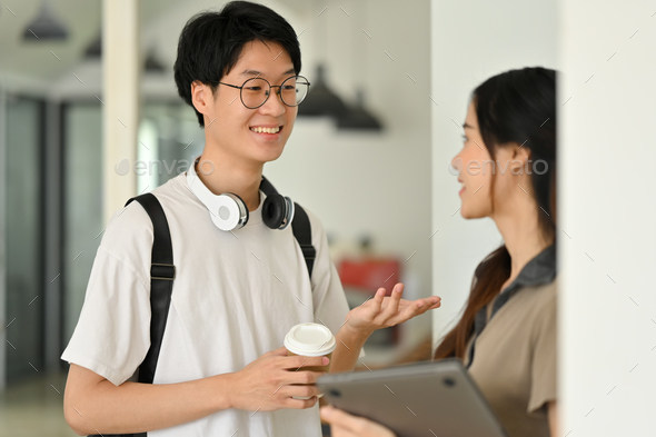 Smiling young student man talking with his classmate while standing at ...