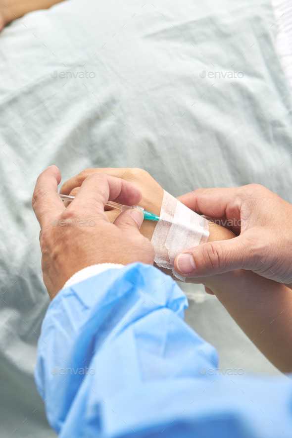 Vertical shot of a doctor connecting an IV drip to a patient's hand ...