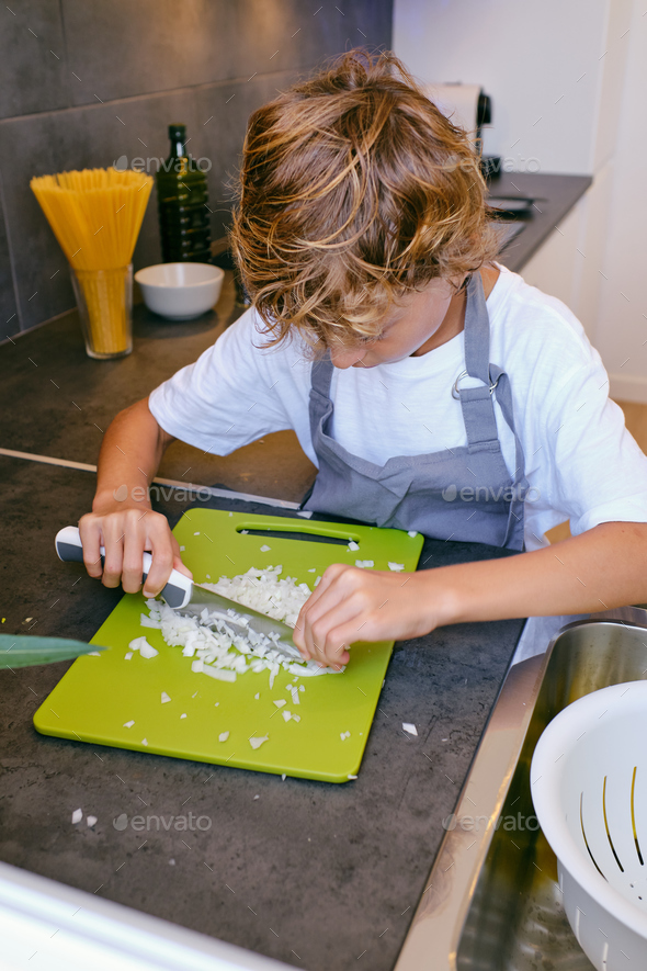Focused boy cutting fresh onion while cooking in kitchen Stock Photo by ...