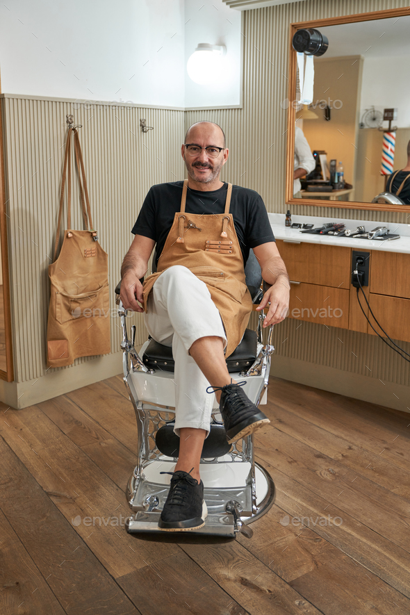 Confident smiling barber sitting on chair in barbershop Stock Photo by ...