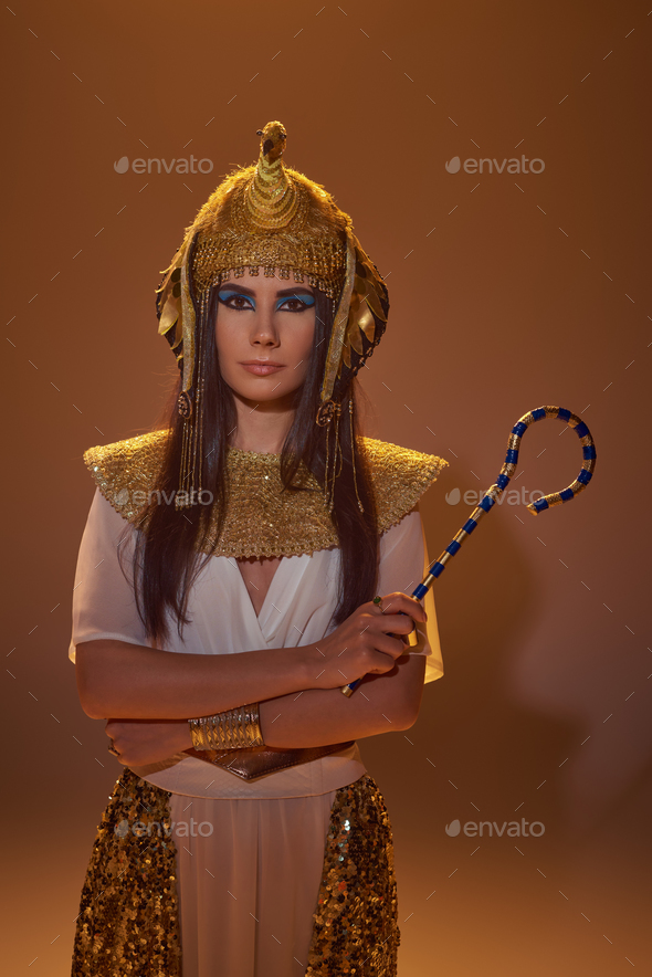 Brunette woman in egyptian attire and headdress holding crook and ...