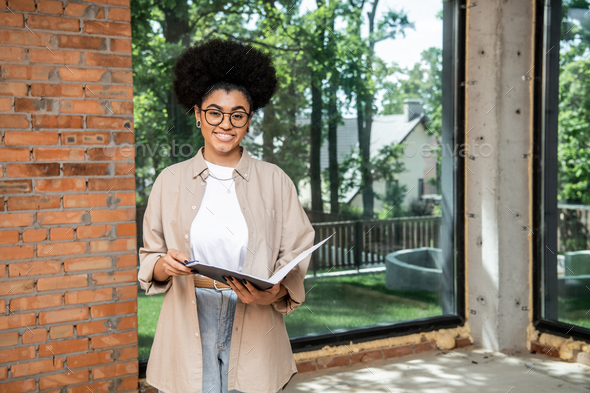 cheerful african american realtor with folder looking at camera in ...