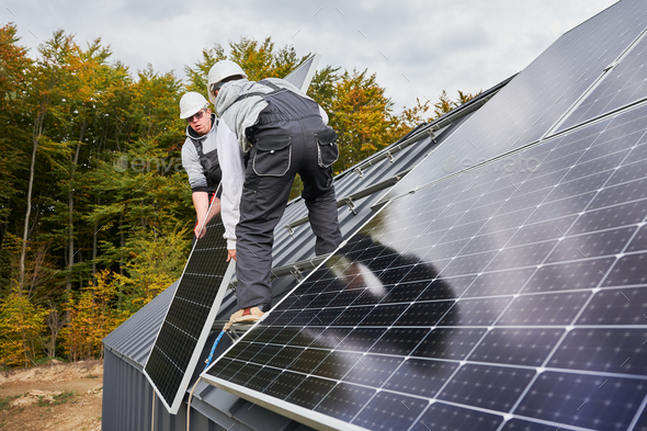 Workers lifting up photovoltaic solar module while installing solar ...