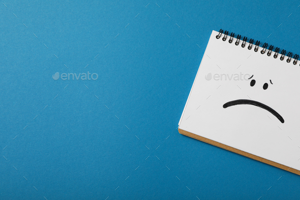 Notepad with sad emoji on blue background, space for text Stock Photo ...