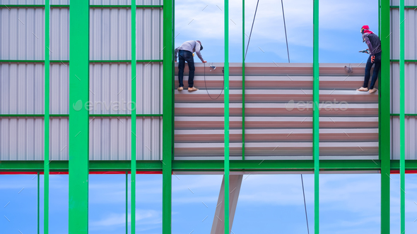 Two workers installing aluminum louver on industrial building structure ...