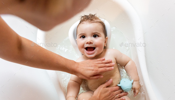 Mom bathing her smiling baby in bathtub Stock Photo by leszekglasner