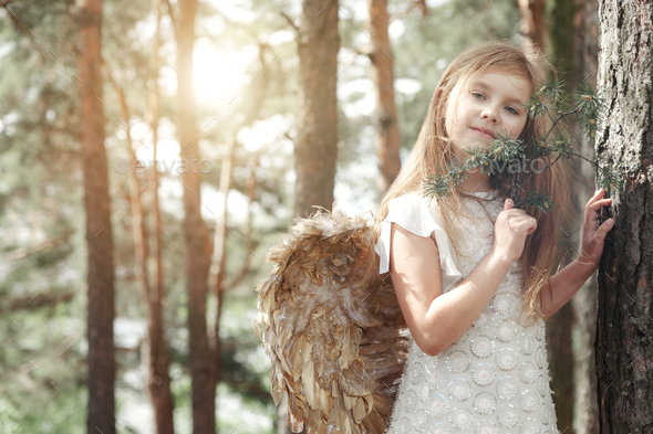 Portrait of little girl in angel image with gold wings standing by tree ...