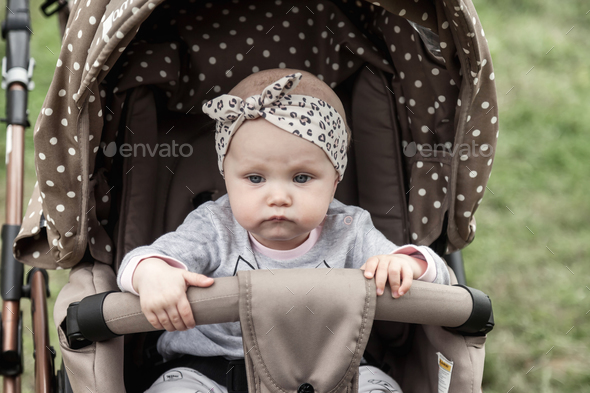 Lonely cute baby with blue eyes sitting in stroller, sad looking away ...