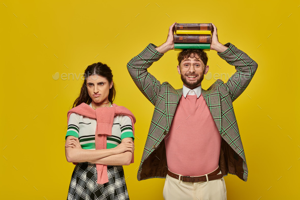 displeased woman standing with folded arms near happy man with books on ...