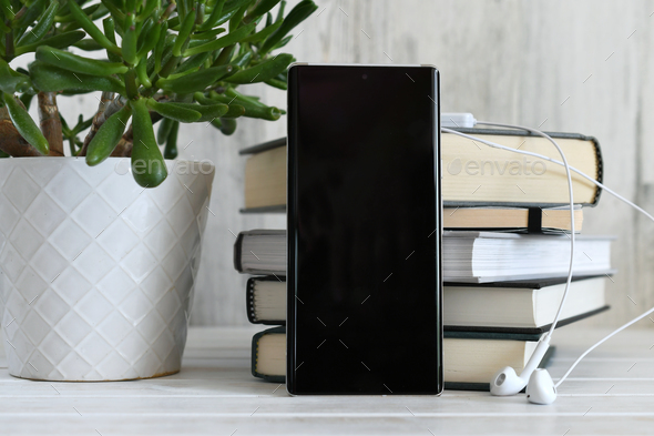 Phone with blank black screen for mock up against stack of books with ...