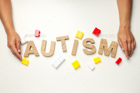 The word "autism" in wooden letters on a light background with legos ...