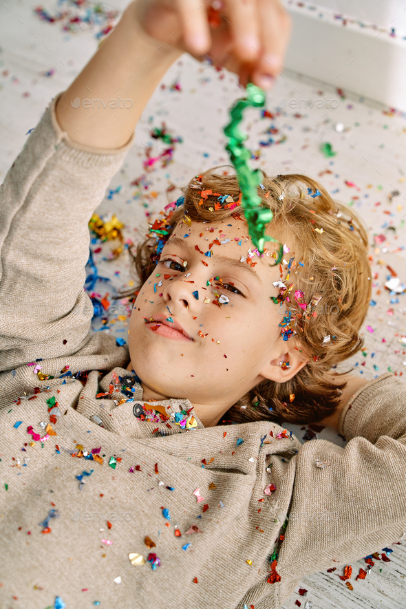 Boy covered with confetti lying on floor Stock Photo by ADDICTIVE_STOCK