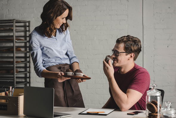 Smiling male and female bakers talking and examining pastries in bakery ...
