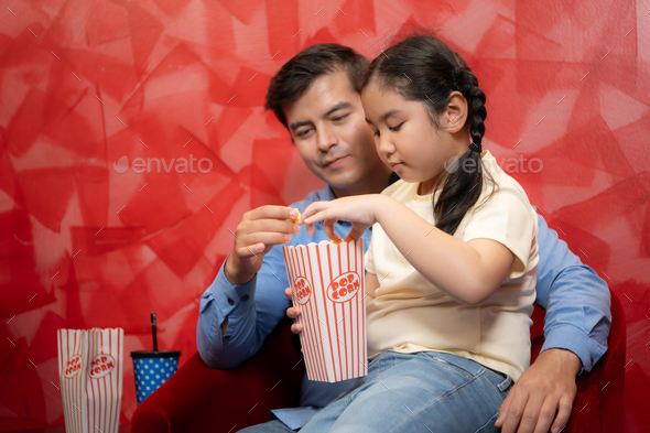 Father and daughter eating popcorn and waiting for watching movie on ...