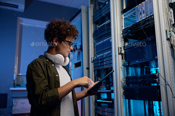 Serious young man working in data center standing at open server rack ...