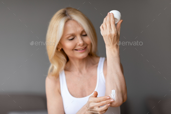 Body care concept. Beautiful middle aged woman rubbing moisturising ...
