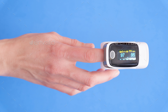 Pulse oximeter on a finger on a blue background Stock Photo by wirestock