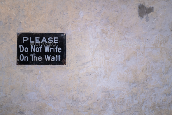 Black warning signboard saying please do not write on the wall in white ...