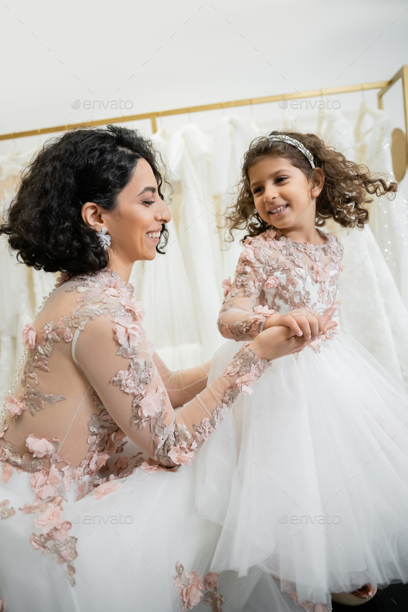 happy middle eastern bride with brunette wavy hair in floral wedding ...