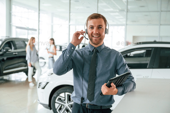 Manager is in the headphones. Handsome car dealership worker is with ...