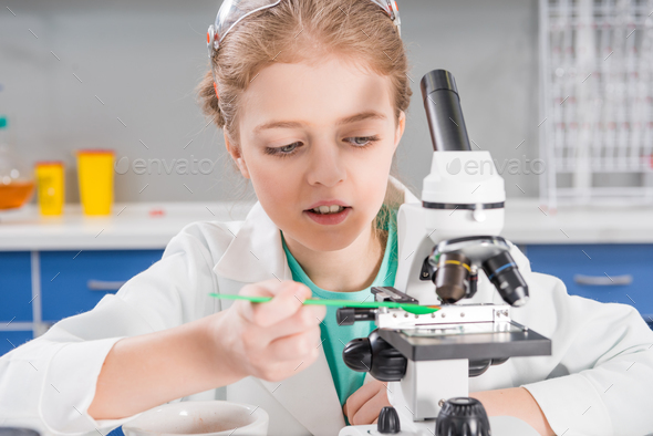concentrated adorable little girl in goggles with microscope in ...
