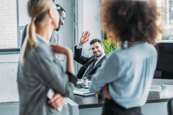 smiling businessman waving hand to multicultural colleagues in office ...