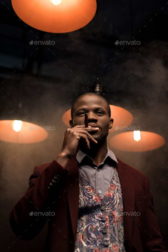 stylish elegant african american man smoking cigar in dark room with lamps Stock Photo by ...