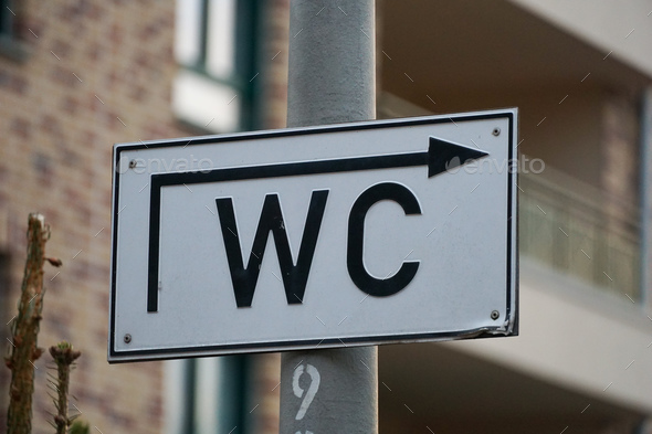 Close up of white WC sign with black letters and right arrow on pillar ...