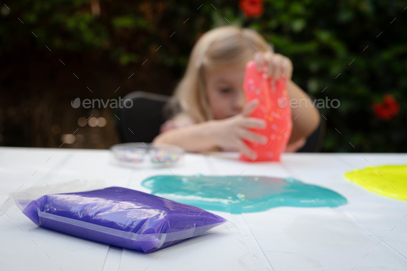 Defocused blonde caucasian girl with playing with slime at desk. Child ...