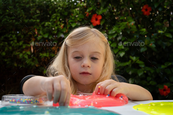 Cute blonde caucasian girl playing with slime, sticky mass at desk ...